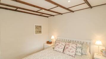 Quarto com cama, duas mesas de cabeceira, mesa de apoio e teto com vigas de madeira.