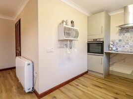 Cozinha com forno embutido, radiador branco e prateleira com utensílios de cozinha.