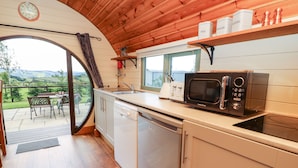 Cozinha compacta com micro-ondas, pia e armários, com vista para uma área externa panorâmica.