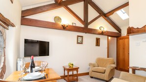 Uma sala de jantar com uma mesa de madeira posta para dois, um sofá e uma televisão fixada na parede.