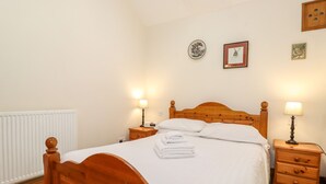 Uma cama bem arrumada com lençóis brancos, duas mesas de cabeceira com abajures, uma cabeceira de madeira e um radiador.