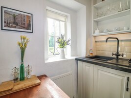 Cozinha com armários brancos, bancada preta, janela com vista para vegetação e um vaso de flores no parapeito.