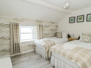 Quarto com duas camas, janela com cortinas, mesa de cabeceira com abajur e quadros nas paredes.