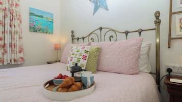 Uma cama bem arrumada com roupa de cama floral, uma decoração em forma de estrela na parede e uma mesa de cabeceira com abajur e tomada.