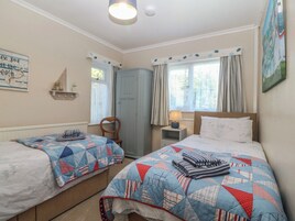 Quarto com duas camas de solteiro, mesa de cabeceira, cadeira, guarda-roupa e janela com cortinas.