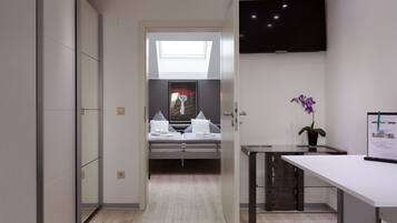 Quarto de hotel moderno com cama, escrivaninha, televisão e claraboia.