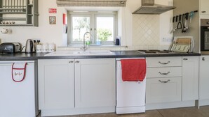 Cozinha moderna com armários brancos, pia de aço inoxidável e janela com vista para áreas verdes.