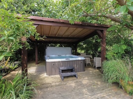 Uma banheira de hidromassagem sob uma pérgola de madeira, rodeada por vegetação exuberante.