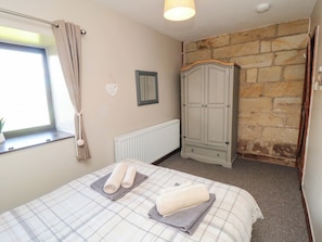 Quarto com cama, guarda-roupa, radiador, janela com cortinas e parede de pedra.