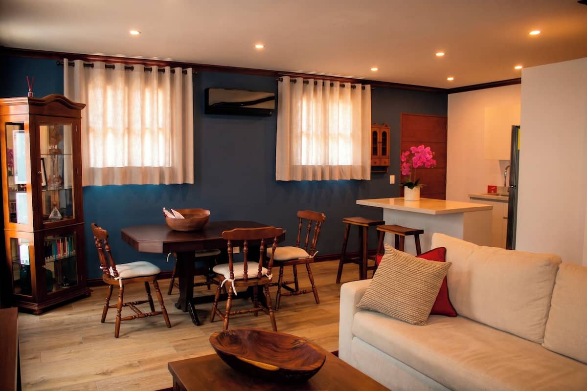 Uma sala de estar com sofá, mesa de jantar, cadeiras, aparador de madeira e armário.
