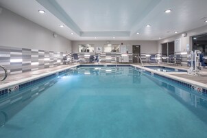 Piscina de hotel com borda azulejada, elevador de piscina e área de estar com cadeiras.