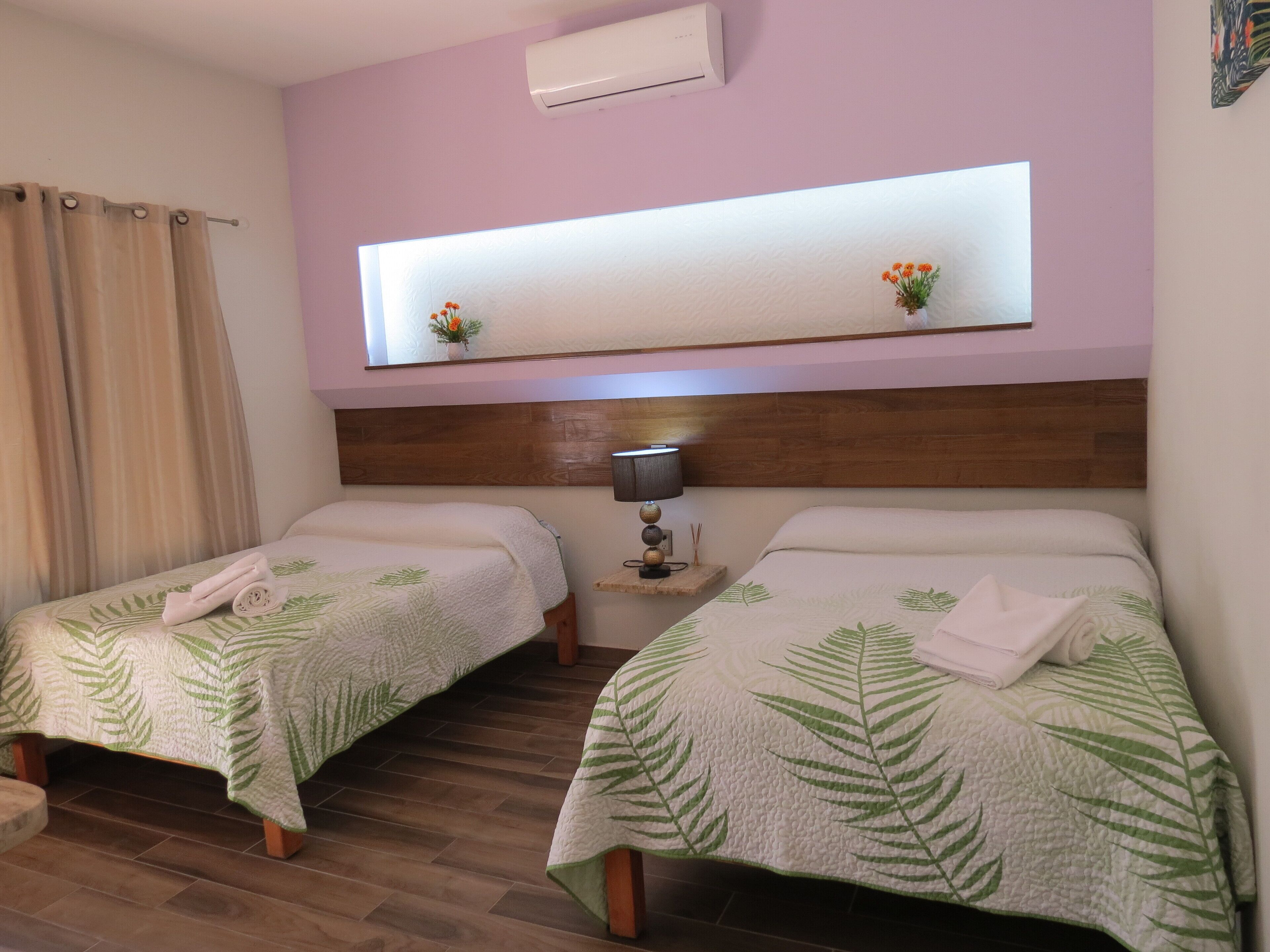 Quarto de hotel com duas camas, um espelho grande e uma mesinha de cabeceira com abajur.