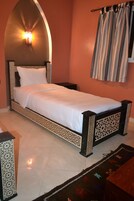 Uma cama com cabeceira estampada, luminária fixada na parede e cortina listrada.