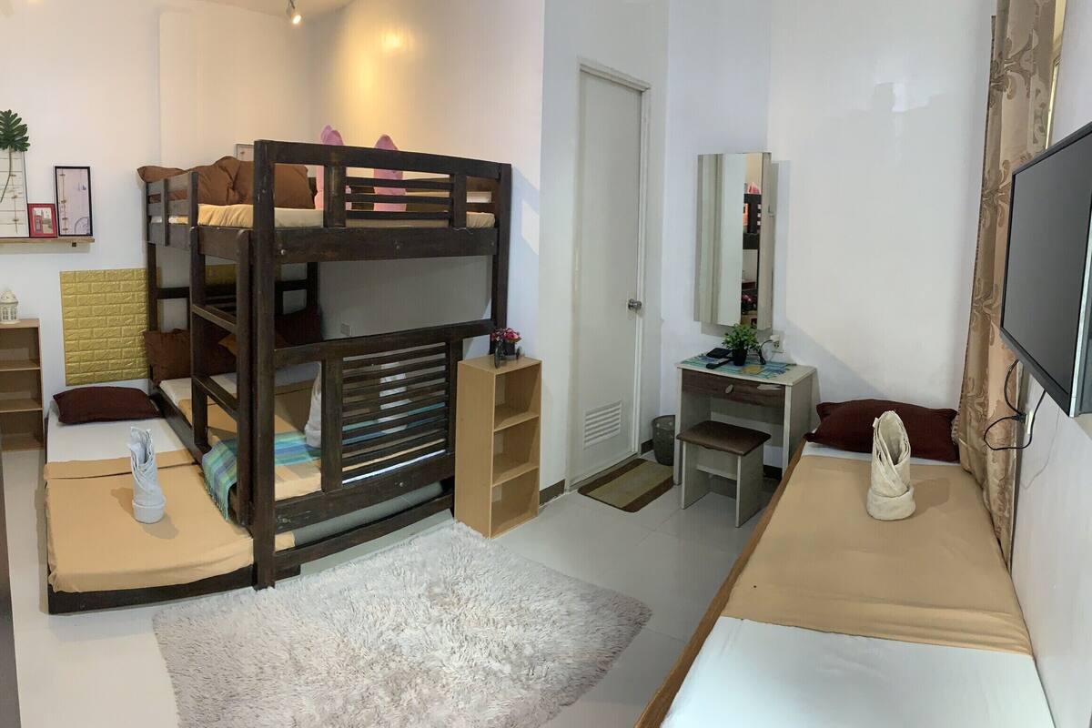 Um quarto com beliches, uma escrivaninha com cadeira, uma televisão e uma pequena estante com objetos decorativos.