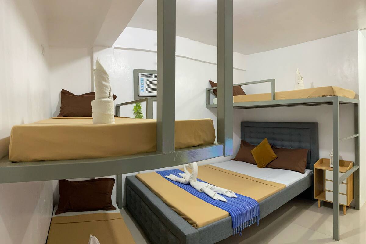 Quarto de dormitório com beliches, uma mesinha de cabeceira e ar-condicionado fixado na parede.