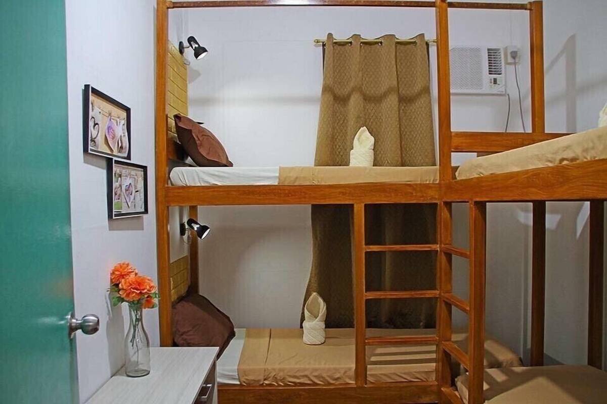 Quarto com beliche de madeira, mesa de cabeceira com um vaso de flores e ar condicionado fixado na parede.