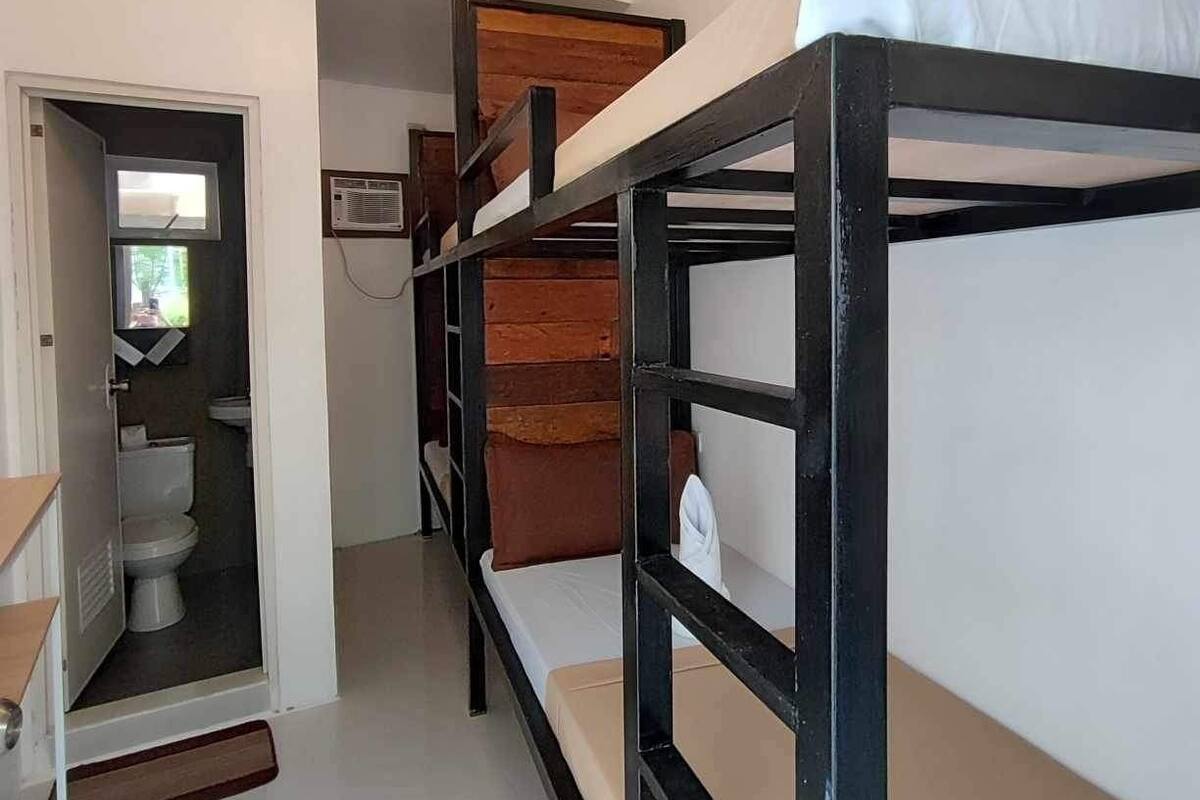 Quarto com beliche, uma escada de madeira, porta branca que dá para um banheiro e luminária no teto.