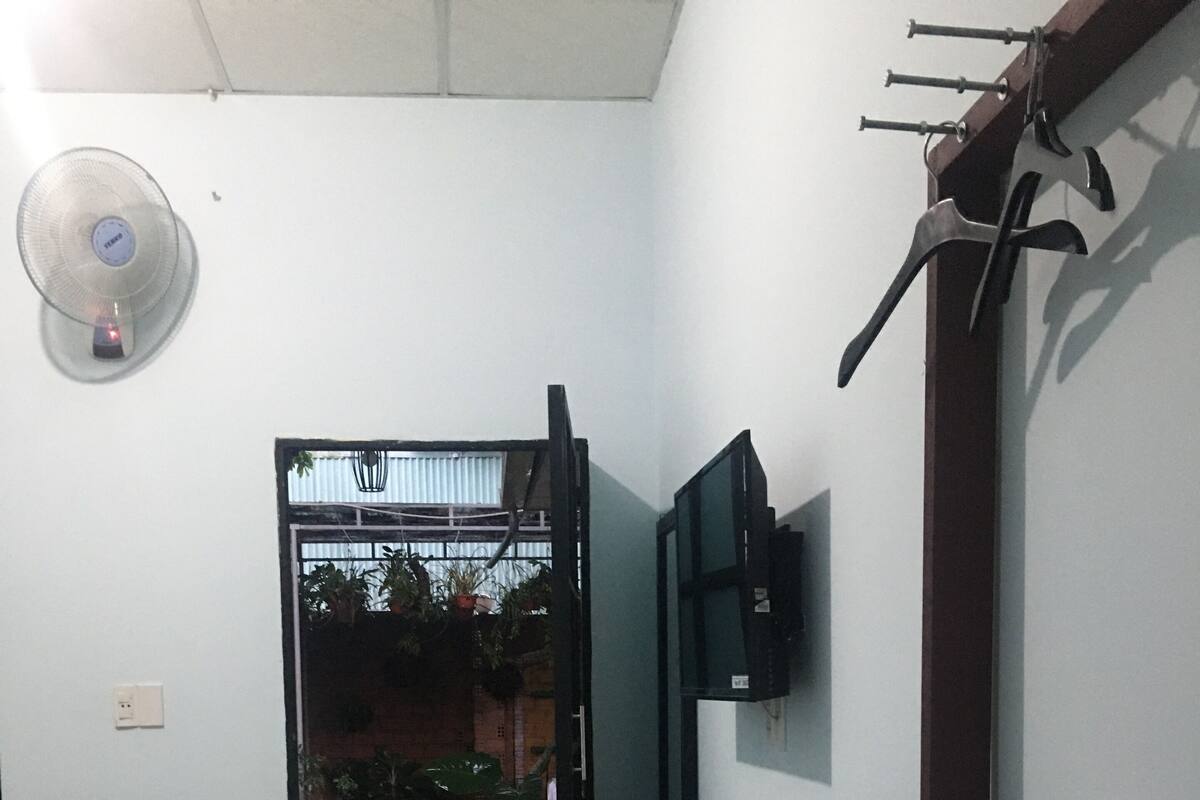Um corredor com uma porta fechada, um ventilador, um bebedouro e uma mesinha com uma planta.