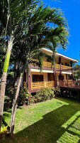 Um edifício de dois andares com varanda, rodeado por palmeiras e um gramado bem cuidado.