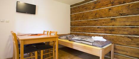 Quarto com cama em madeira estilo banco, mesa de jantar de madeira com cadeiras e televisão de tela plana na parede.