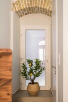 Um corredor com uma porta branca, um vaso com planta de folhas verdes e frutos amarelos, e um banco de madeira.