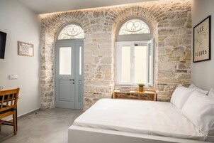 Quarto com parede de pedra, uma cama, uma janela e uma porta.