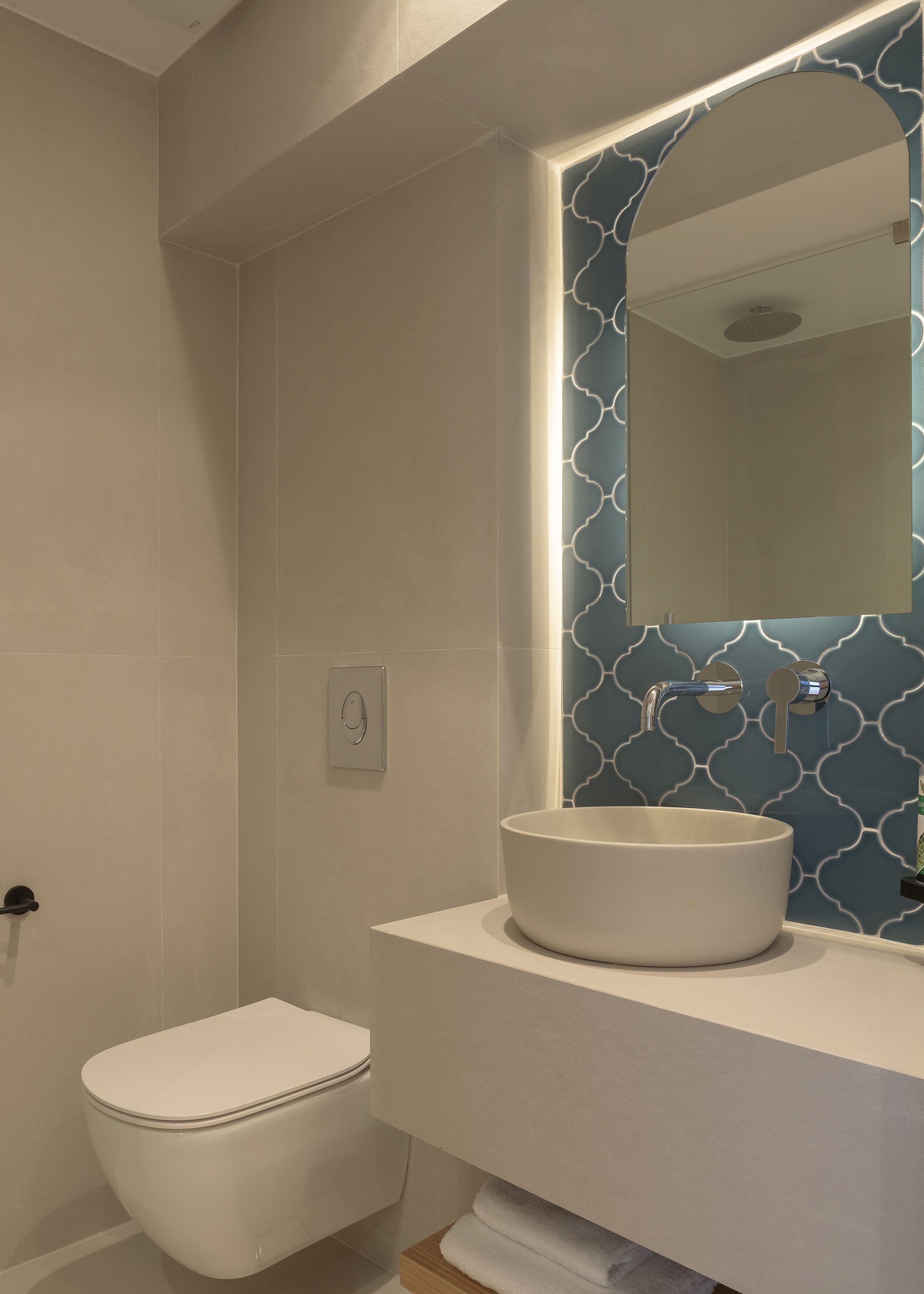 Casa de banho com sanita branca, lavatório branco com espelho grande e parede com padrão azul.