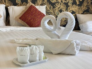 Quarto de hotel com cama, almofadas, bandeja com toucas de banho e toalhas dispostas em formato de coração.
