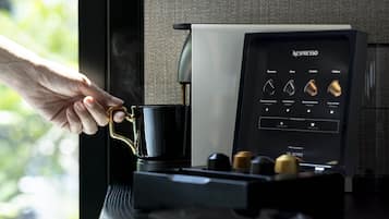 Uma mão segurando uma xícara de café perto de uma máquina de café Nespresso.