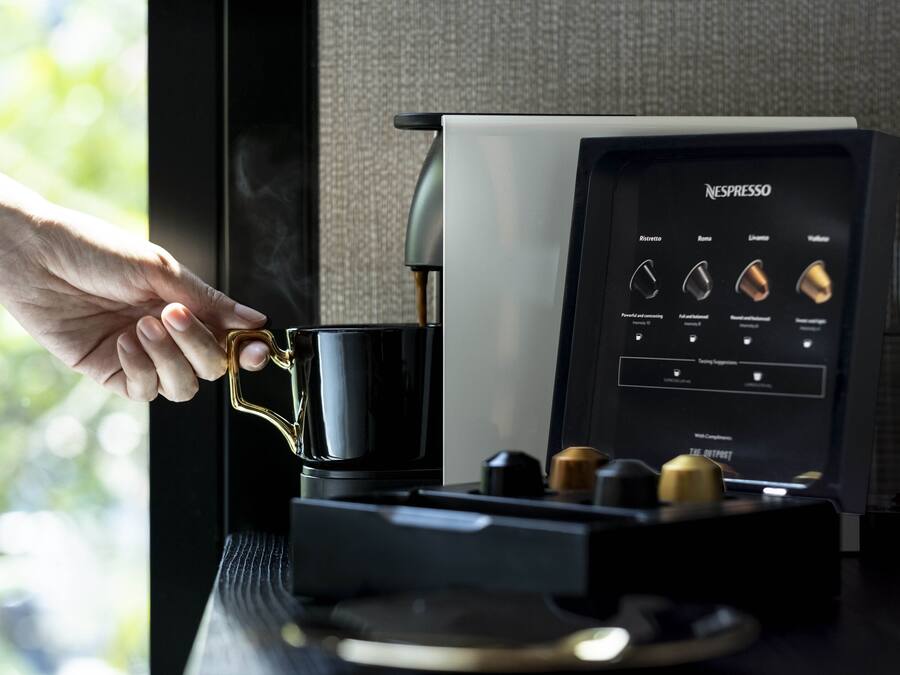 Uma mão segurando uma xícara de café perto de uma máquina de café Nespresso.