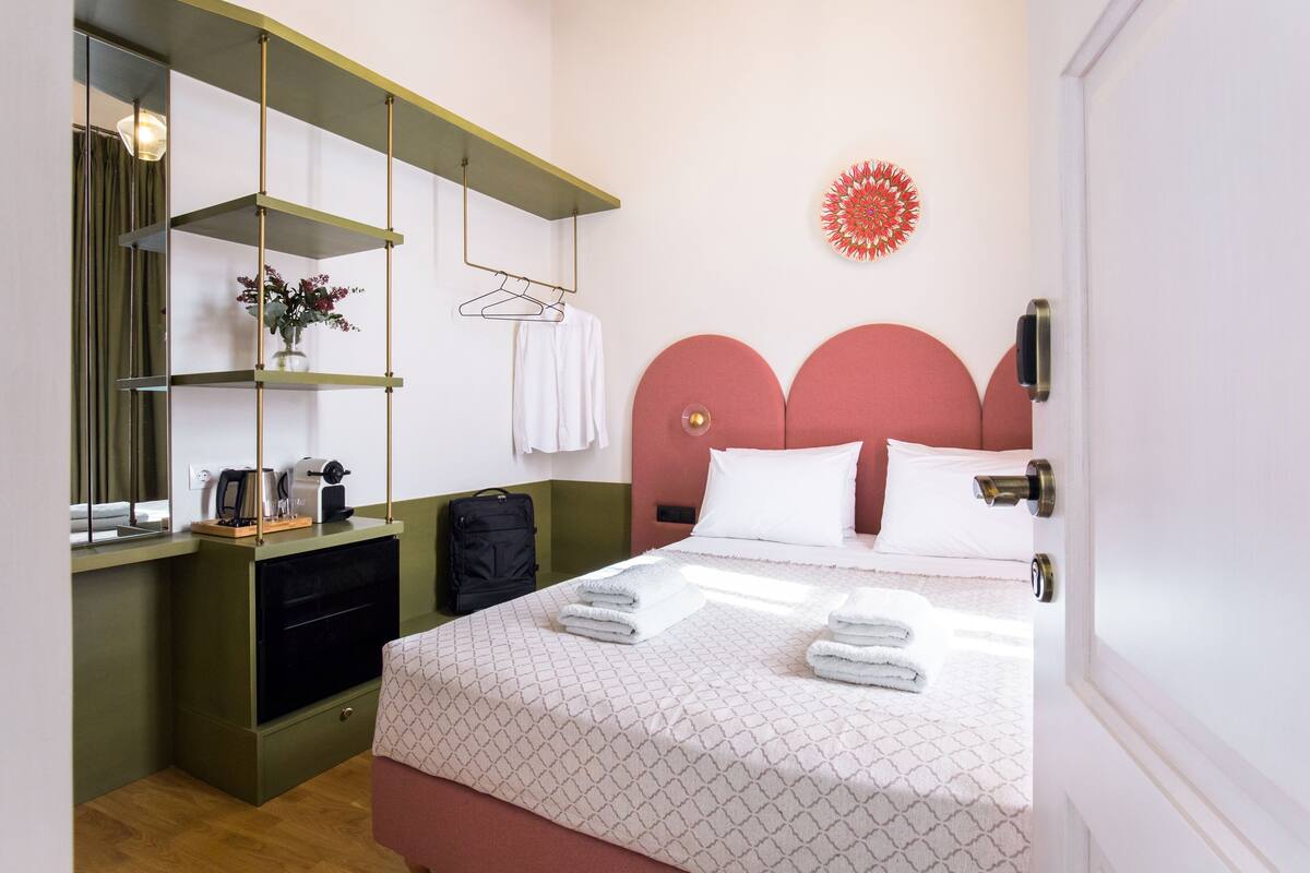 Quarto de hotel com uma cama, espelho, prateleira com um vaso e decoração na parede.