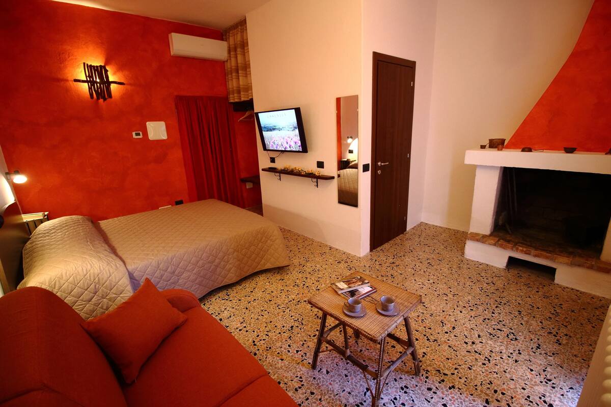 Quarto de hotel com cama, sofá, televisão, lareira e uma pequena mesa com objetos.