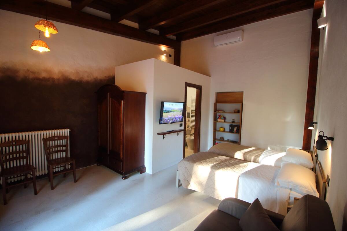 Quarto com duas camas, um guarda-roupa de madeira, um radiador e uma televisão na parede.