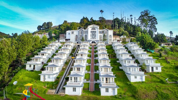 Um grande resort com várias villas brancas dispostas em fileiras numa encosta, um caminho central e um parquinho.