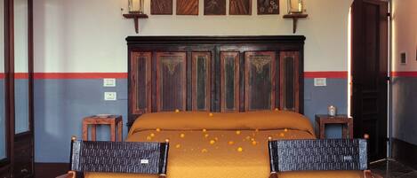 Quarto de hotel com uma cama grande, duas poltronas, uma mesa pequena e uma parede decorativa com obras de arte emolduradas.