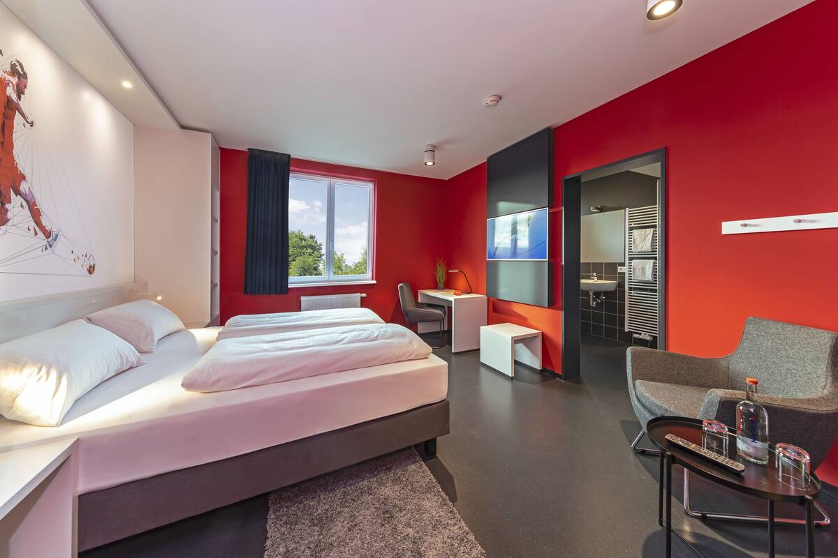 Quarto de hotel moderno com uma cama grande, uma mesa de escritório, uma cadeira e uma televisão.