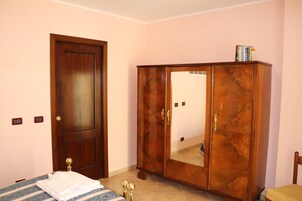 Quarto com guarda-roupa de madeira, cama com colcha listrada e uma cadeira.