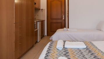 Quarto de hotel com cama, tapete estampado, guarda-roupa de madeira, kitchenette e luminária suspensa.