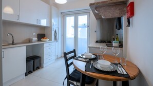 Cozinha moderna com armários brancos, uma mesa de jantar posta com pratos, copos e talheres, e vista para a varanda pela porta.