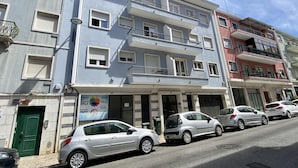 Um edifício com várias andares, varandas, uma porta verde e carros estacionados.