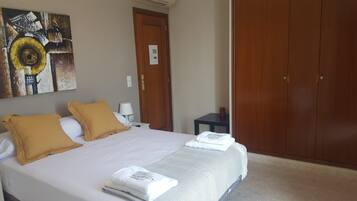 Quarto de hotel com uma cama, duas almofadas, mesa de cabeceira, luminária, quadro, porta e guarda-roupa.