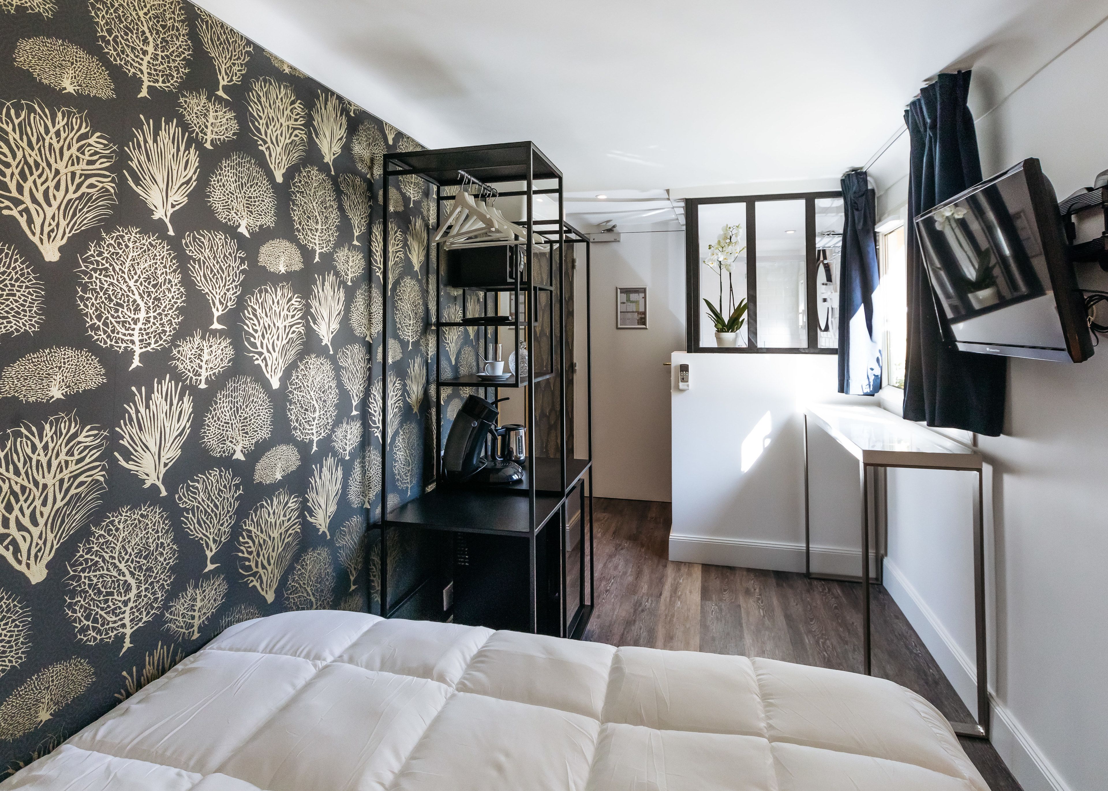 Quarto com cama, estante preta, escrivaninha branca e televisão fixada na parede.