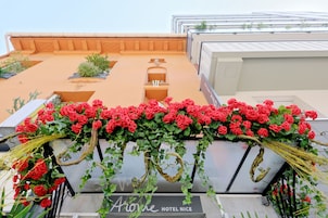Exterior de hotel com um grande arranjo de flores vermelhas e uma placa com a inscrição "Aroine HOTEL NICE".