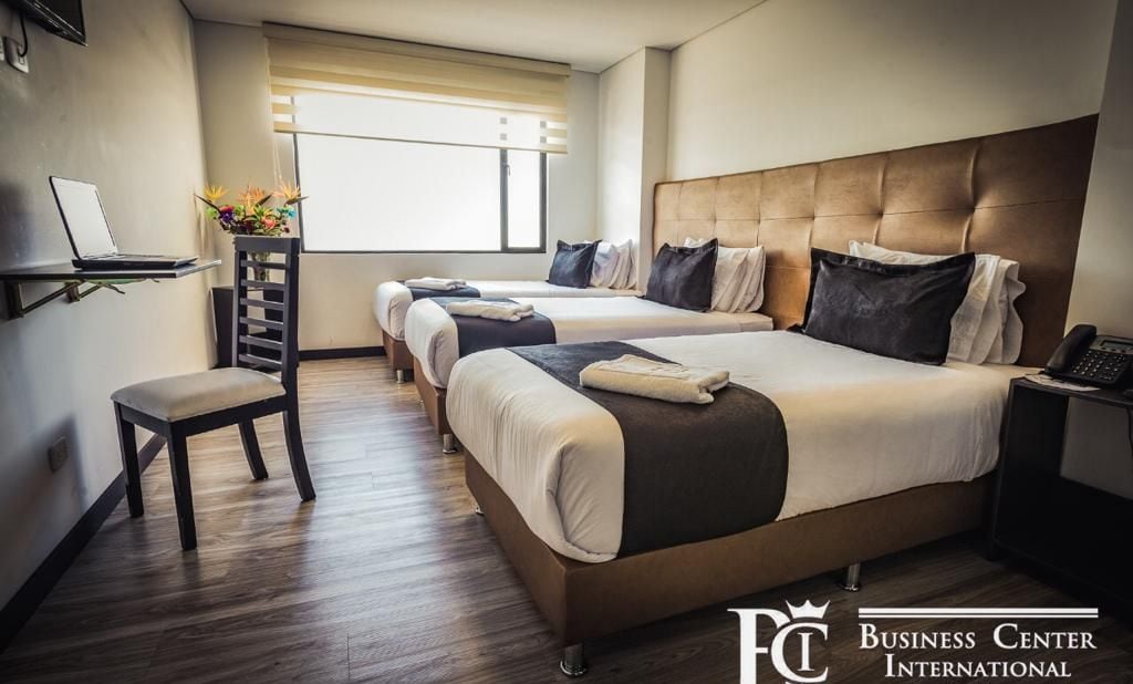 Quarto de hotel com duas camas, uma escrivaninha com um laptop, uma cadeira e uma mesa de cabeceira com um telefone.