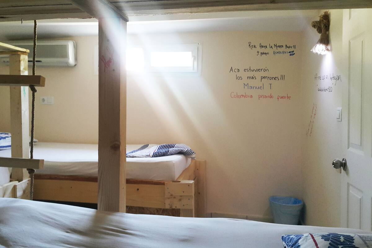 Quarto de dormitório com beliches, uma lousa com anotações manuscritas e uma janela que oferece luz natural.