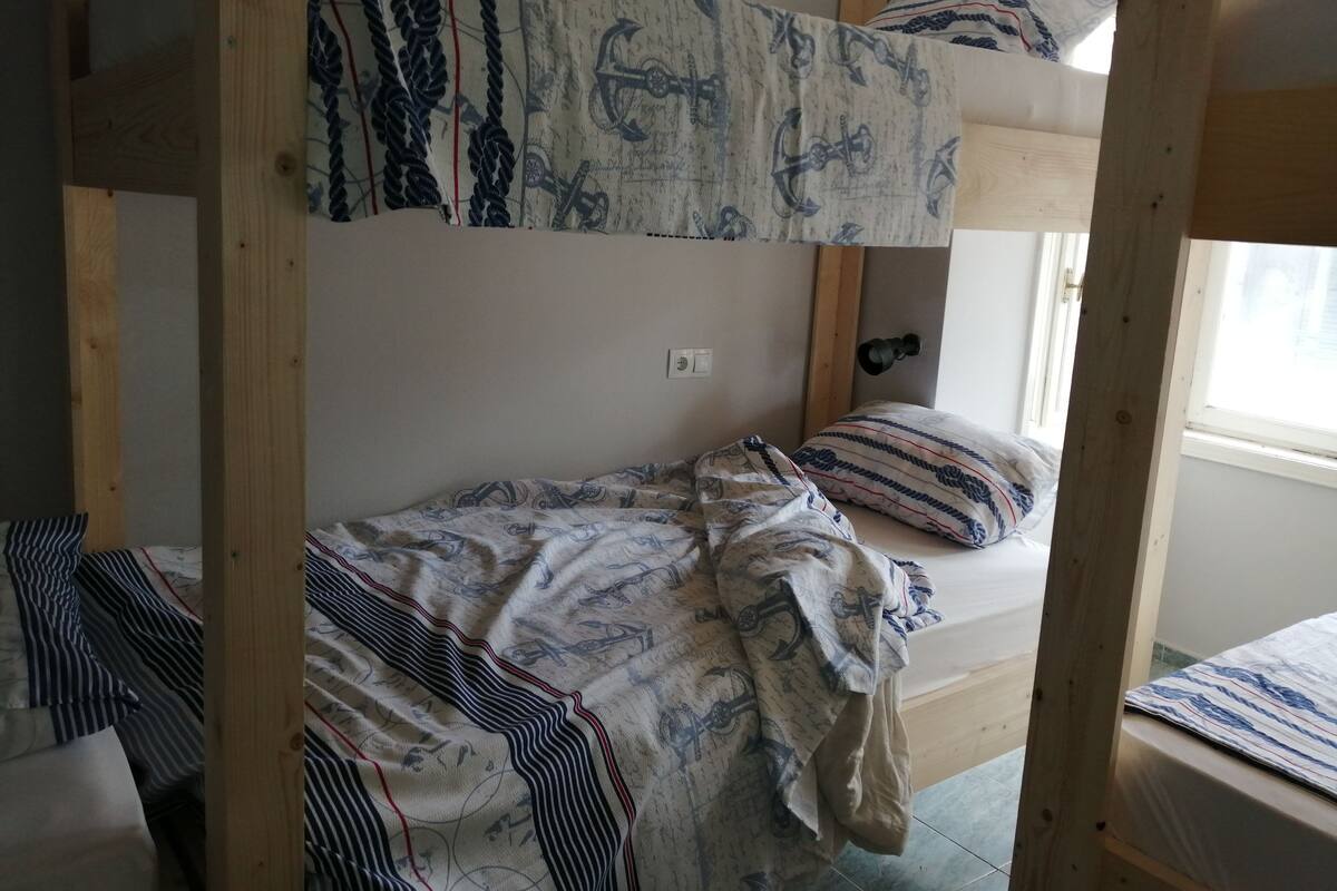 Quarto com beliche, colcha estampada, luminária de cabeceira e janela.