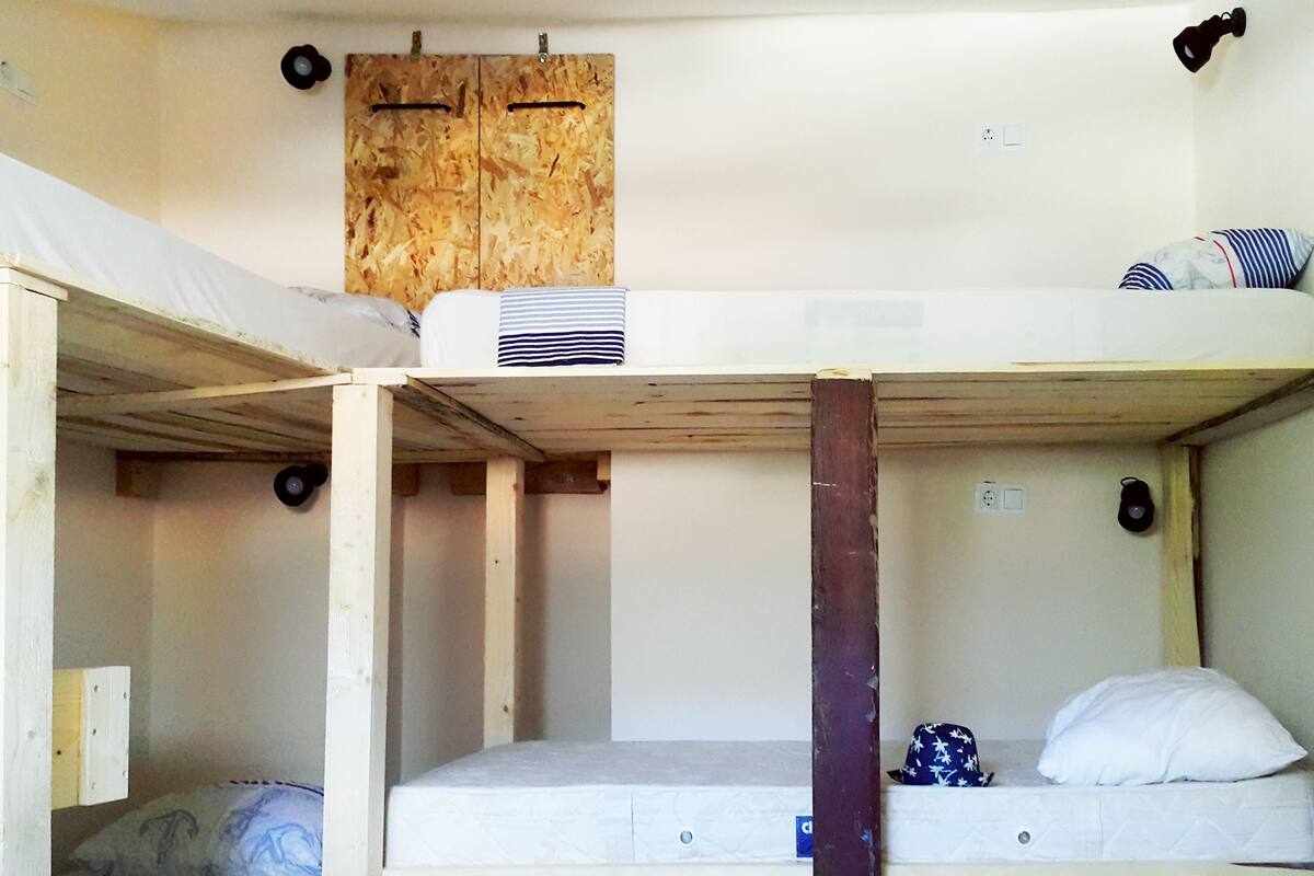 Quarto com beliche, cabeceira de madeira, prateleira pequena e luminária fixada na parede.