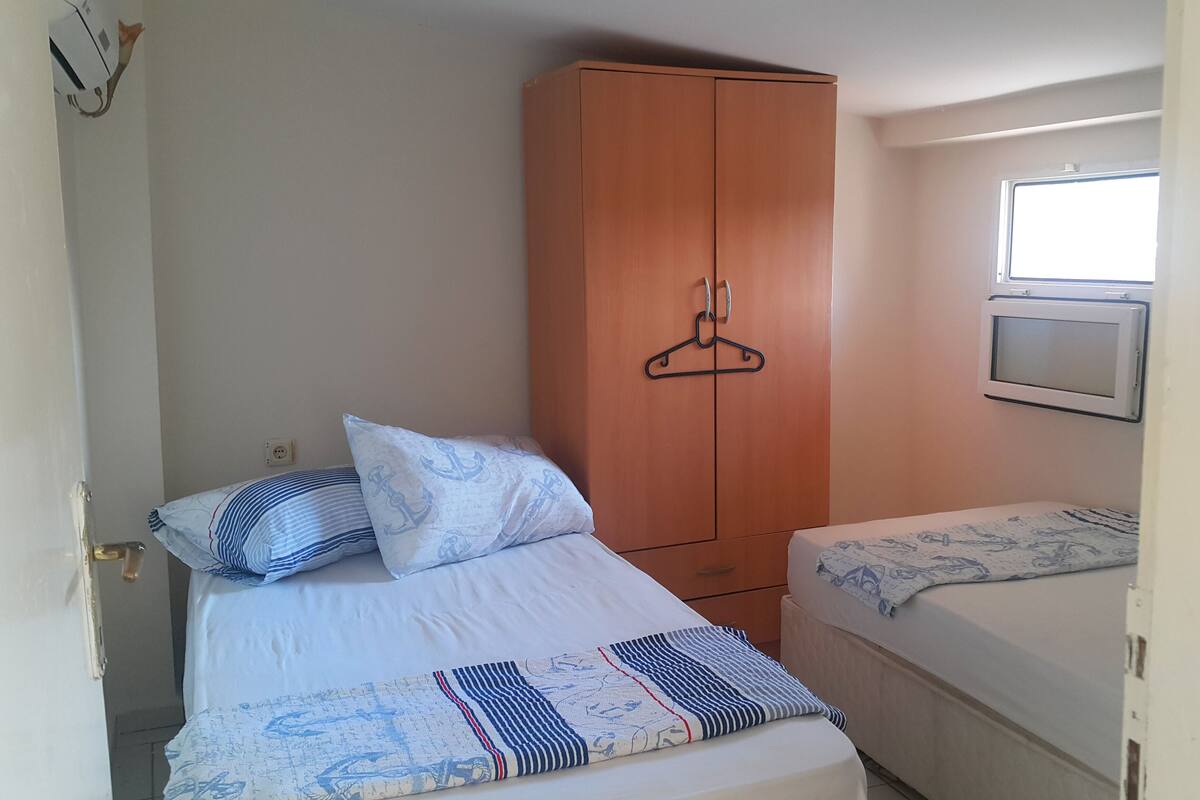 Quarto com duas camas, guarda-roupa, televisão e janela.