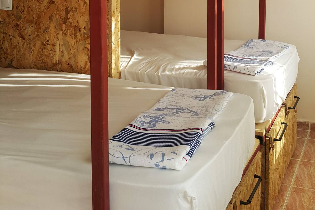 Uma cama beliche com roupa de cama branca e cobertores listrados, cabeceira de madeira e pés de metal.