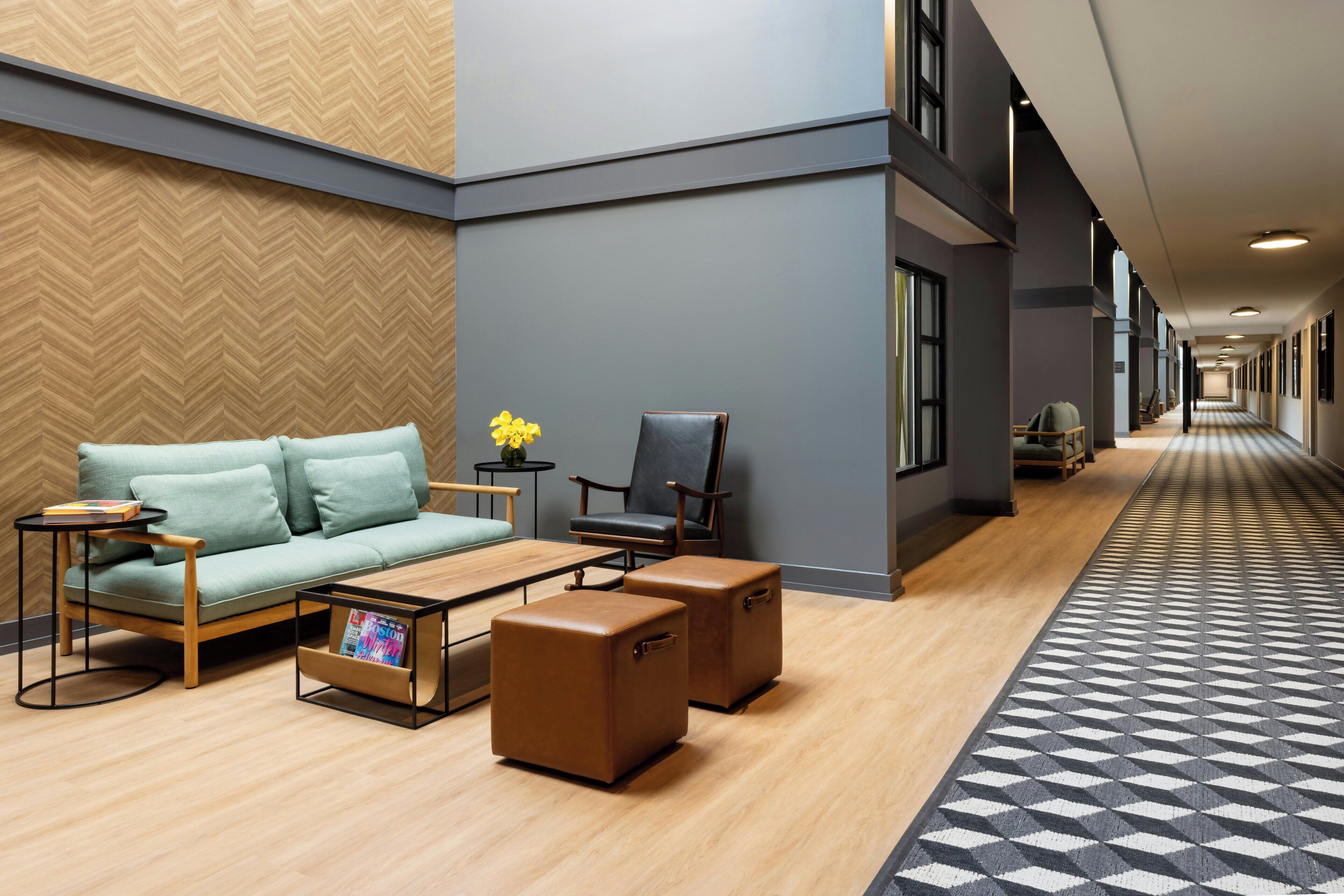 Um hall de hotel moderno com um sofá, poltronas, uma mesa de centro e um tapete estampado.